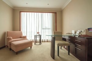 Quarto de hotel com sofá, mesa de vidro, escrivaninha e cadeira.
