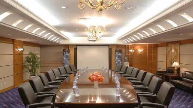 Uma sala de conferência com uma mesa comprida, cadeiras de couro preto, um candelabro e um arranjo floral.