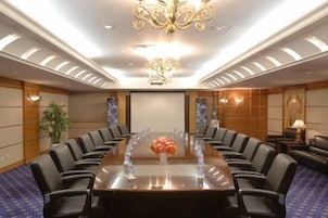Uma sala de conferência com uma mesa comprida, cadeiras de couro preto, um candelabro e um arranjo floral.
