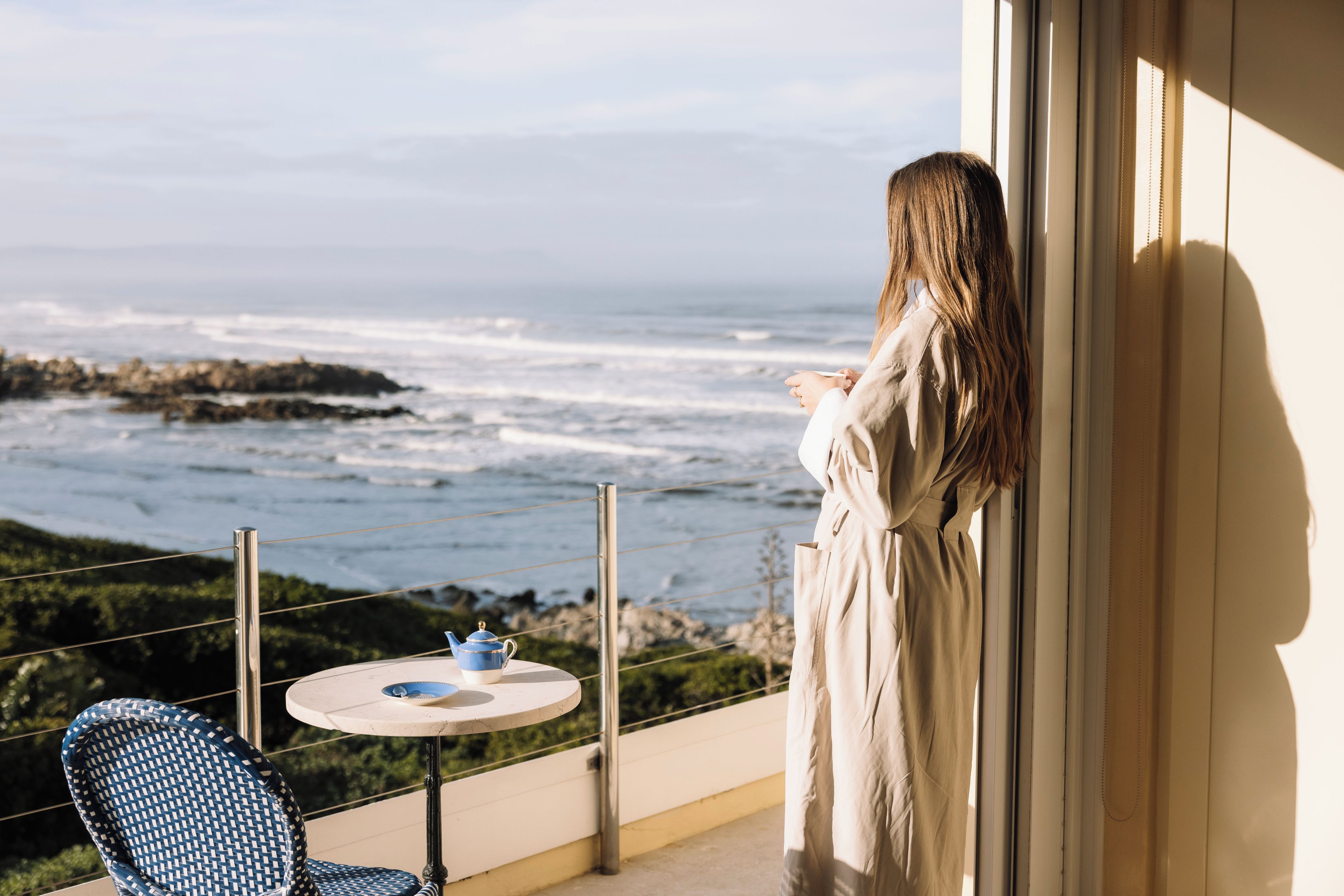 Uma varanda com vista para o oceano, uma mesa com um bule e uma cadeira.