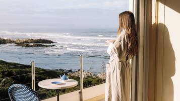 Uma varanda com vista para o oceano, uma mesa com um bule e uma cadeira.