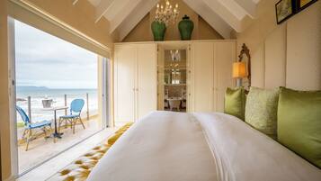 Quarto com uma cama grande, uma varanda com mesa e cadeiras, e vista para o mar.