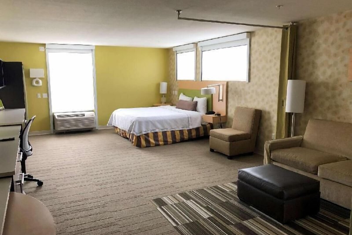 Quarto de hotel com cama, duas poltronas, sofá, escrivaninha e abajur.