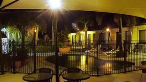Uma área de pátio externa com piscina, cercada por grade e vasos de plantas.