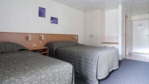 Quarto de hotel com duas camas, um guarda-roupa, uma mesinha e uma porta que dá para outro cômodo.