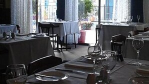 Restaurante com várias mesas preparadas para refeições, oferecendo vista do exterior através de grandes janelas.