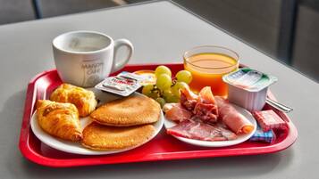 Bandeja de café da manhã com croissants, presunto, queijo, uvas, suco de laranja e uma xícara de café.