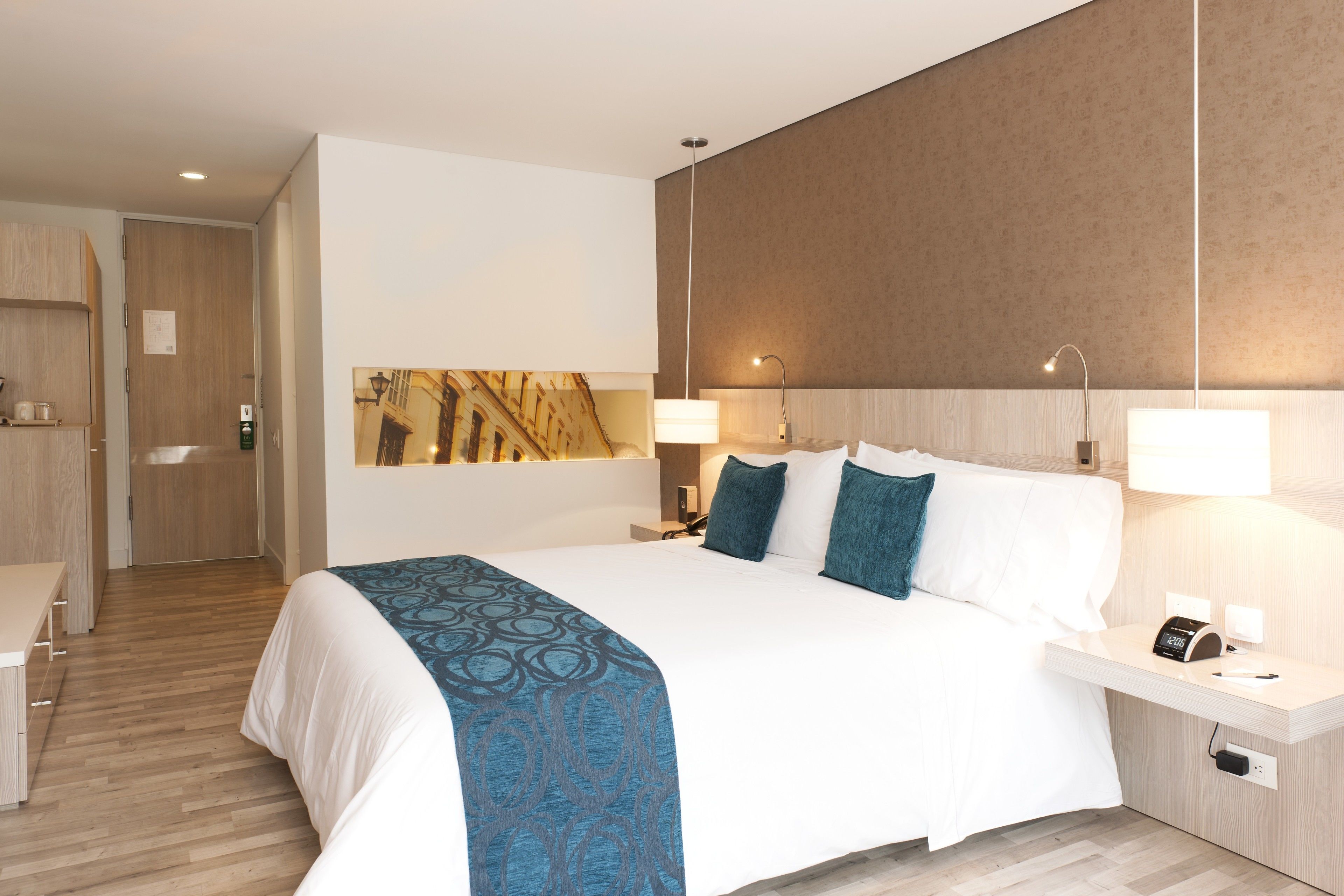 Quarto de hotel moderno com uma cama grande, mesas de cabeceira e um criado-mudo com relógio.