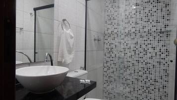 Casa de banho moderna com uma grande pia branca, sanita e cabine de duche em vidro com mosaicos.