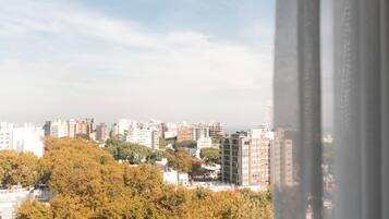 Vista urbana com edifícios e árvores, vista através de uma janela com cortinas.