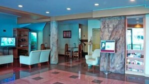 Um hall de hotel com uma TV, área de estar e balcão de recepção.