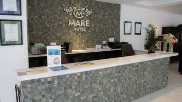 Balcão de recepção de hotel com parede de azulejos, certificados emoldurados e um logotipo.