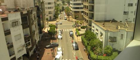 Vista da rua com prédios, carros e pedestres.
