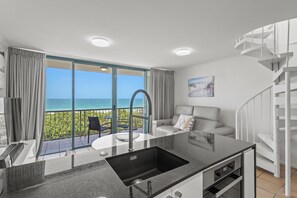 Cozinha moderna com vista para o oceano, área de jantar com mesa e cadeiras, e uma escada.