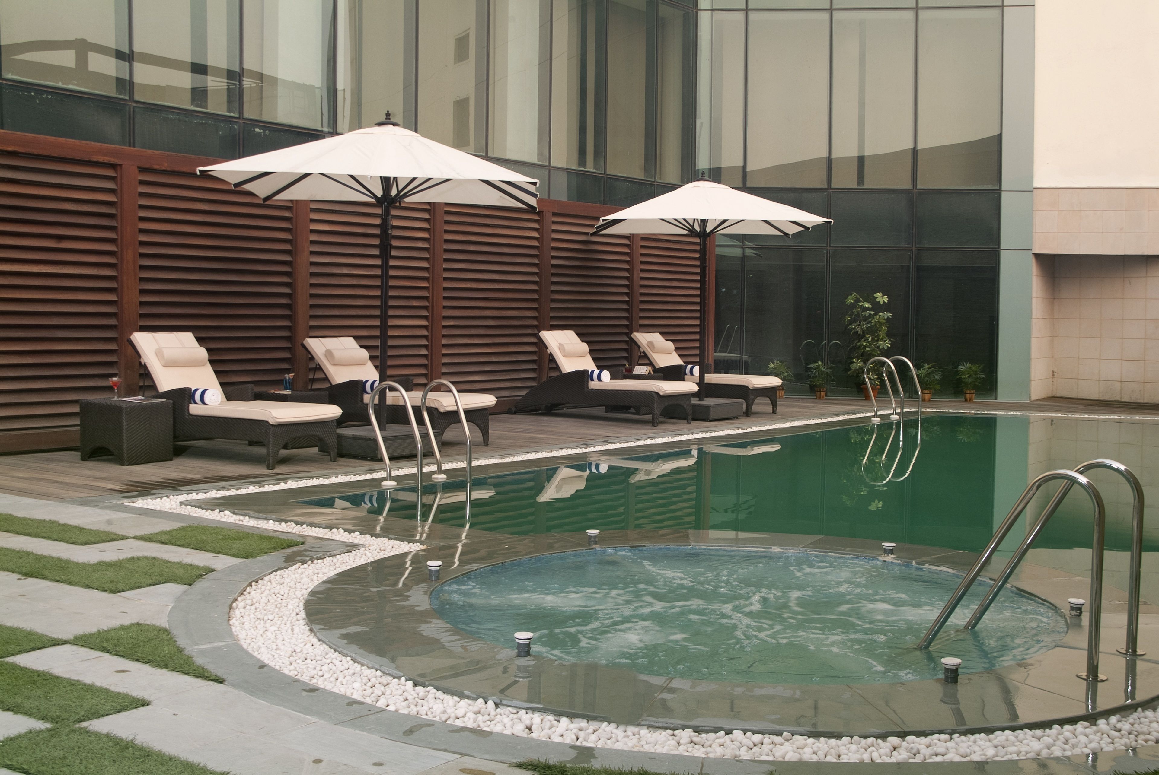 Área de piscina com espreguiçadeiras e guarda-sóis, emoldurada por um edifício moderno com amplas janelas.