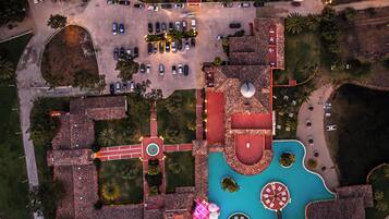 Vista aérea de um resort com piscina, quadra de tênis e várias áreas de estacionamento.