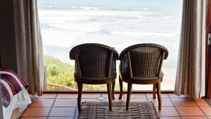 Um quarto com duas cadeiras de vime voltadas para uma grande janela com vista para o oceano.