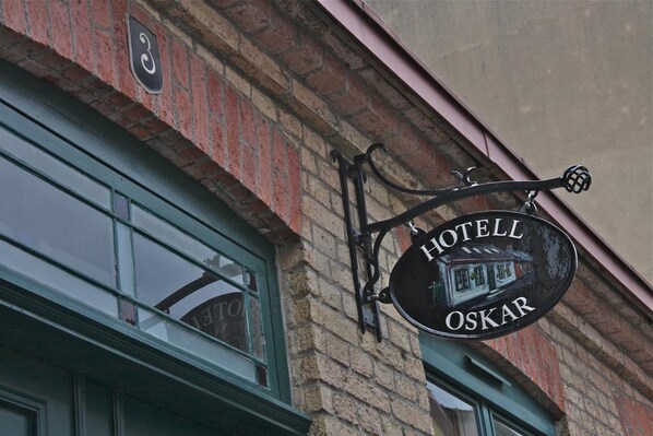 Placa de hotel com o nome 'HOTELL OSKAR' e o número '3' em cima, fixada numa construção de tijolo.