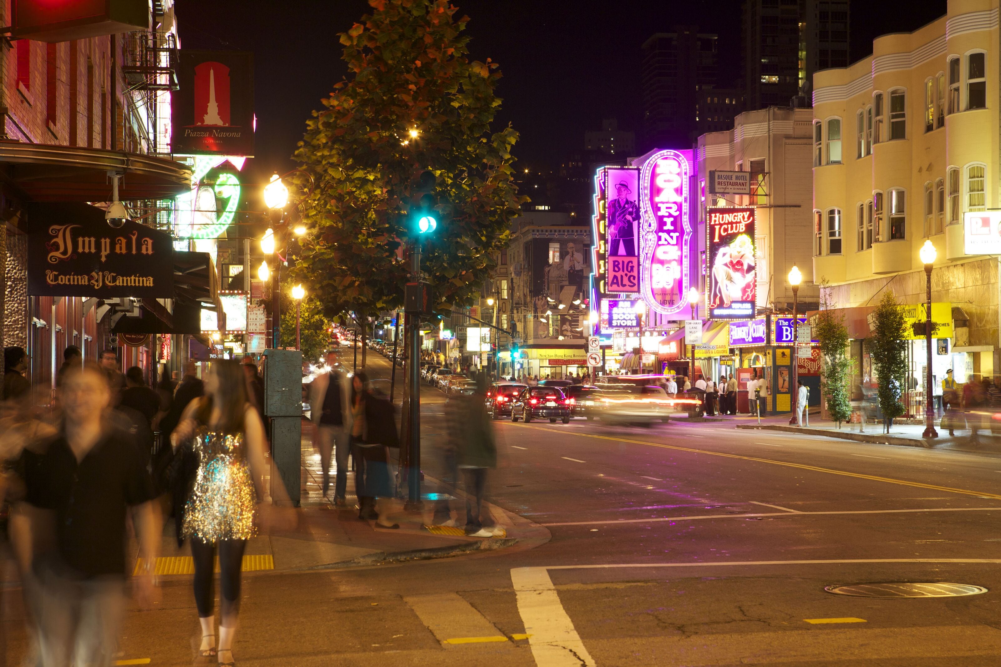 Rua movimentada na cidade à noite, com letreiros e edifícios iluminados.