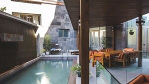 Uma área interna de piscina moderna com mesa e cadeiras de madeira, plantas em vasos e uma parede de pedra.