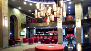 Um saguão com assentos vermelhos, área de bar e luminárias pendentes.