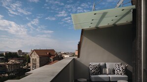 Terraço no telhado com um sofá e dois banquinhos redondos, com vista para a paisagem urbana.
