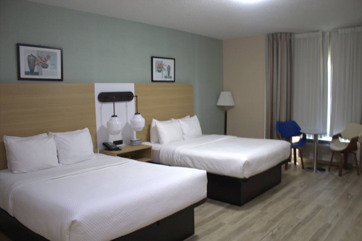Quarto de hotel com duas camas, uma escrivaninha, uma cadeira e duas luminárias fixadas na parede.