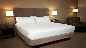 Quarto de hotel com uma cama grande, duas mesas de cabeceira, uma cadeira e duas luminárias fixadas na parede.