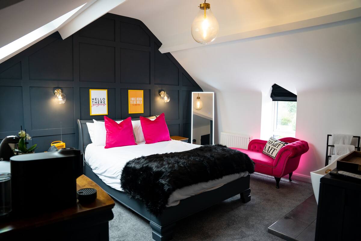 Quarto moderno com cama grande, sofá vermelho e manta felpuda preta e branca.