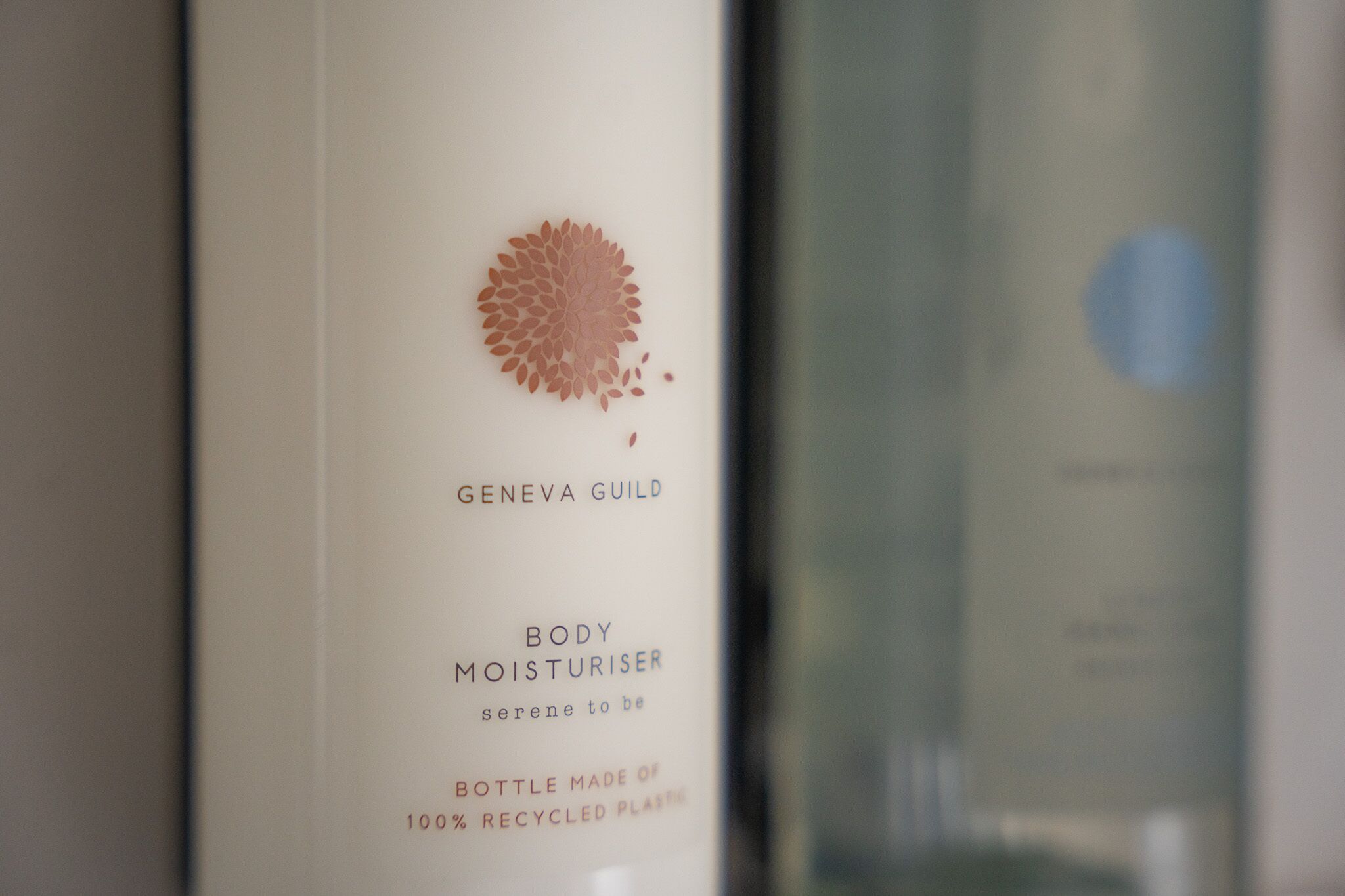 Um frasco de creme hidratante corporal Geneva Guild, com design floral e indicação de ser feito de plástico 100% reciclado.