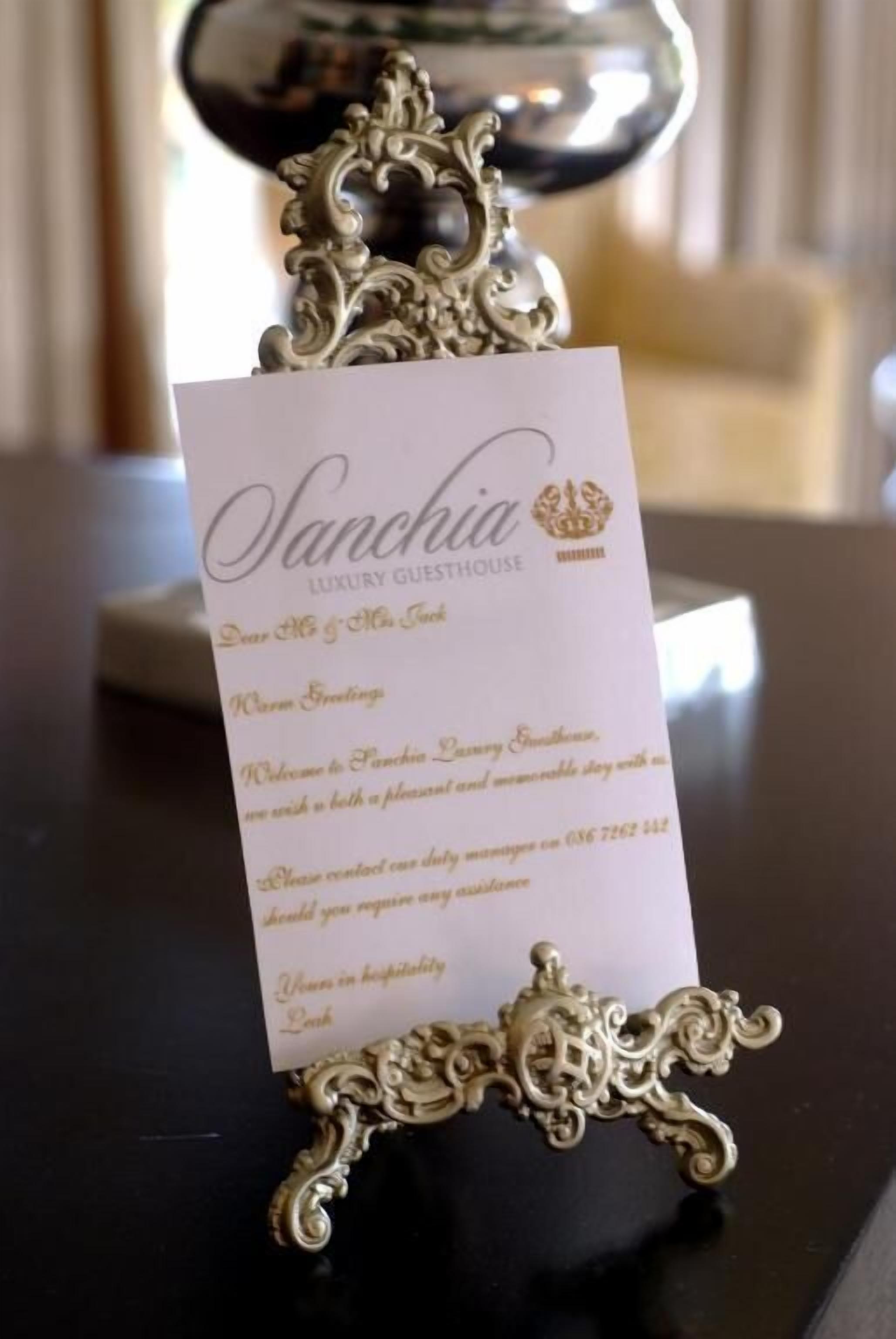 Cartão de visita do 'Sanchia Luxury Guesthouse' com um suporte decorativo.