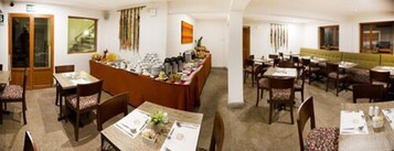 Uma sala de jantar de hotel com várias mesas e cadeiras, um buffet central e uma área de estar com um sofá.