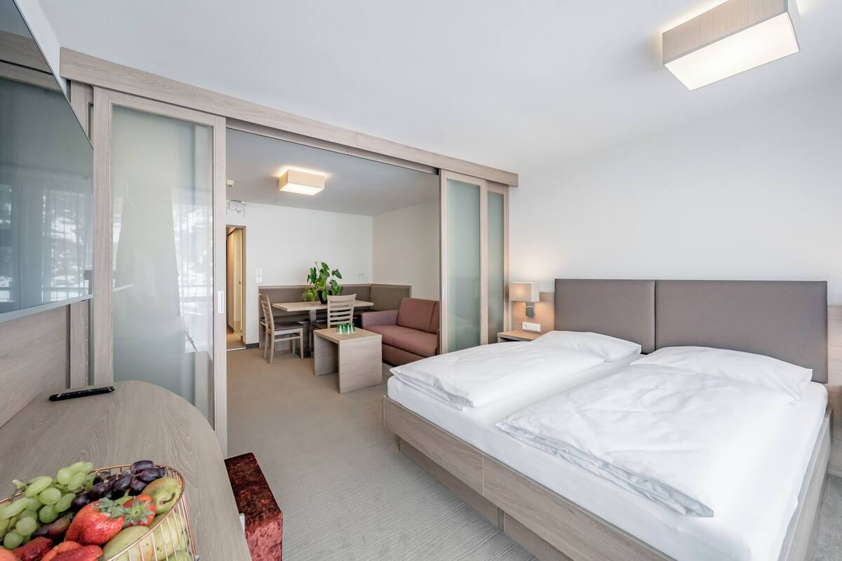 Quarto de hotel com cama, escrivaninha, cadeira e cesta de frutas.