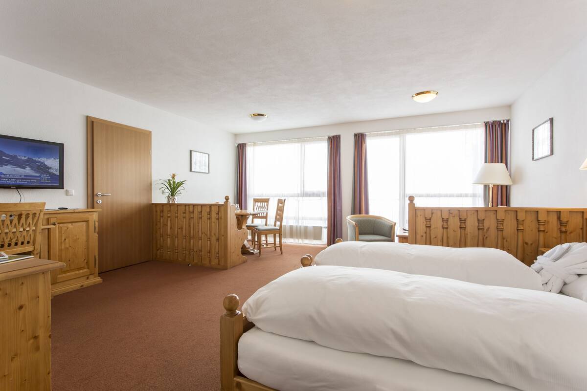 Quarto de hotel com cama, escrivaninha, cadeira e televisão.
