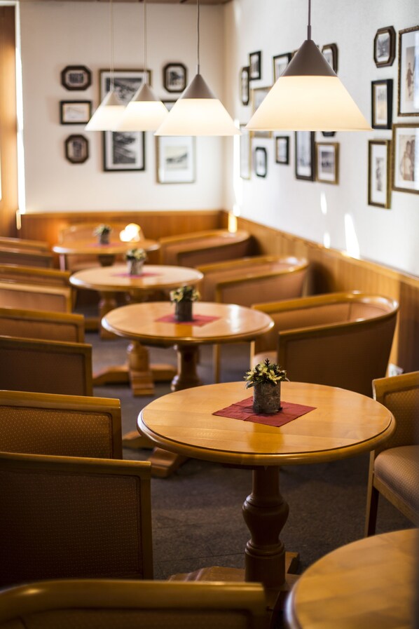 Interior de restaurante com mesas e cadeiras redondas, iluminação pendente e quadros nas paredes.
