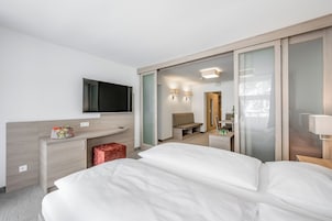 Quarto de hotel moderno com uma cama grande, uma escrivaninha com televisão de tela plana, uma área de estar e uma porta deslizante que dá para um banheiro.