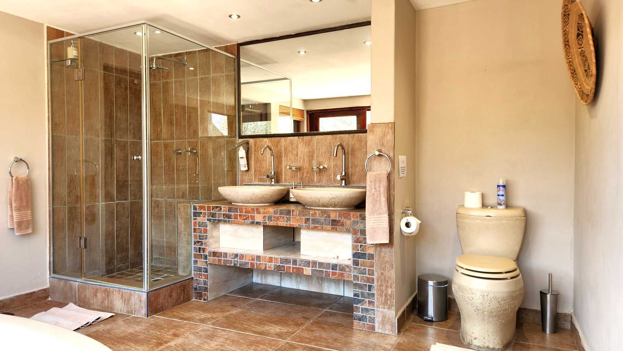 Um banheiro com chuveiro em box de vidro, pia com painel de azulejos e vaso sanitário.