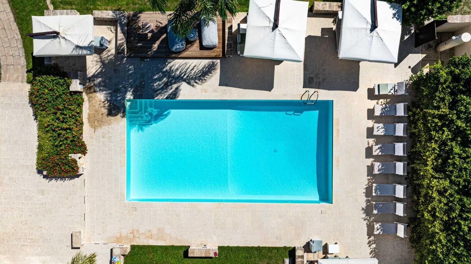 Vista aérea de uma piscina retangular com espreguiçadeiras e guarda-sóis ao redor.