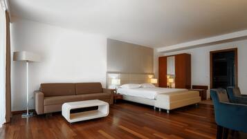 Quarto de hotel moderno com chão de madeira, um sofá, uma cama, uma escrivaninha e uma cadeira.