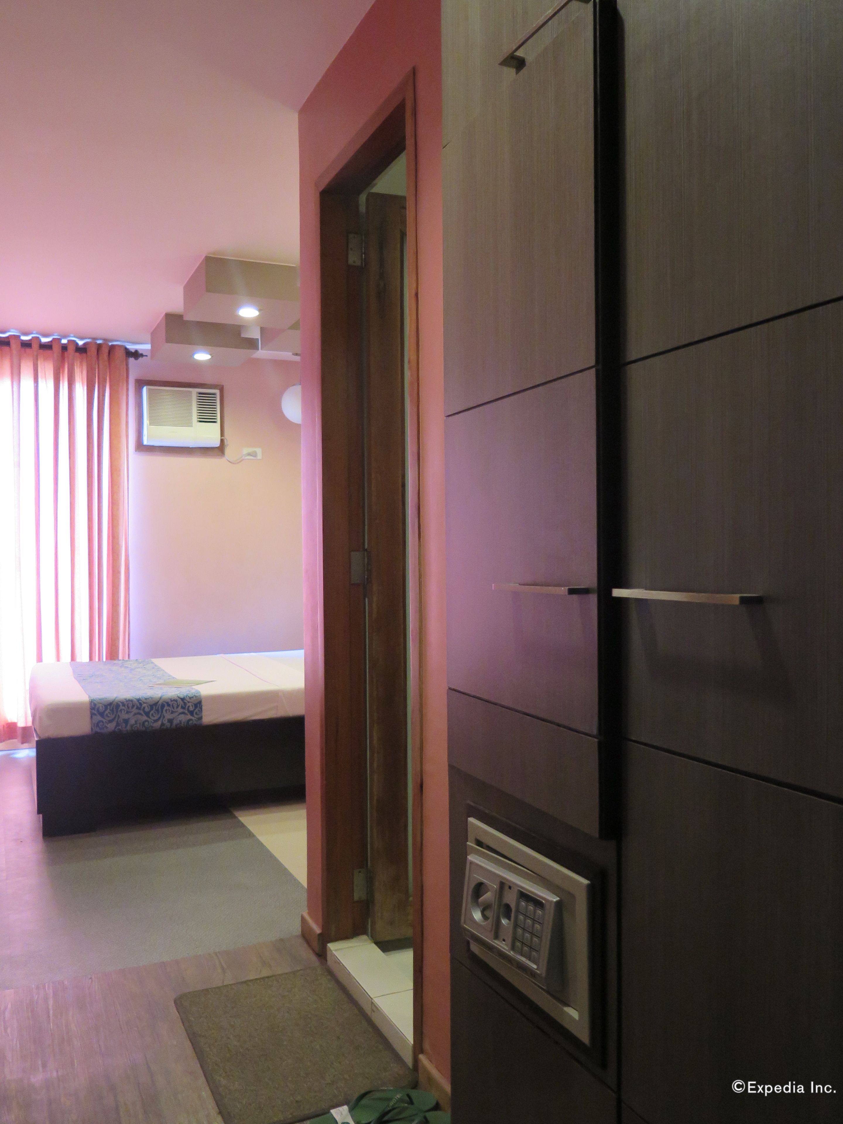 Quarto de hotel com uma cama, um guarda-roupa, um espelho e uma pequena janela com unidade de ar condicionado.