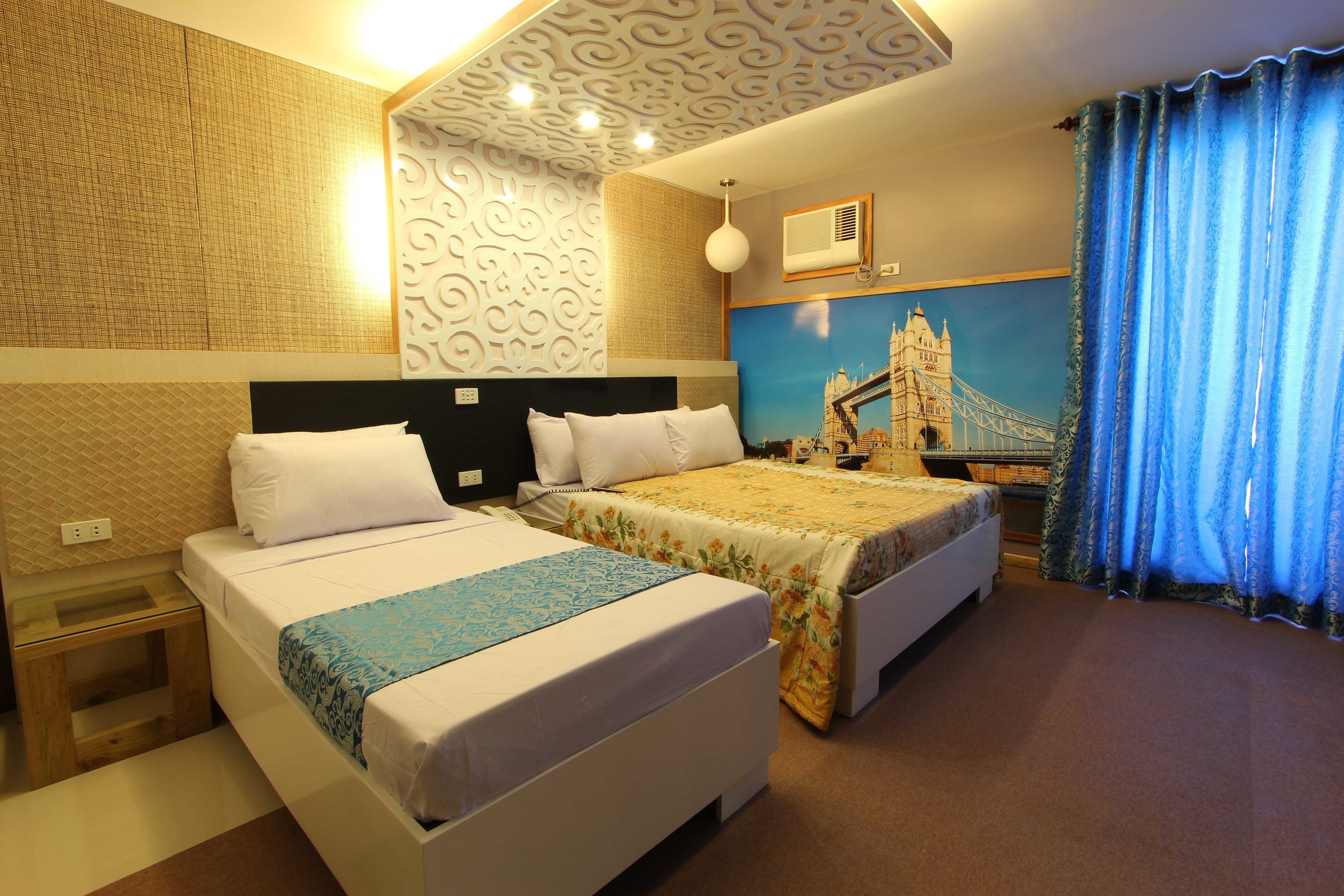 Quarto de hotel com duas camas, um mural de uma ponte e uma janela com cortinas azuis.
