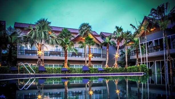 Um hotel com piscina, palmeiras e o reflexo do edifício na água.