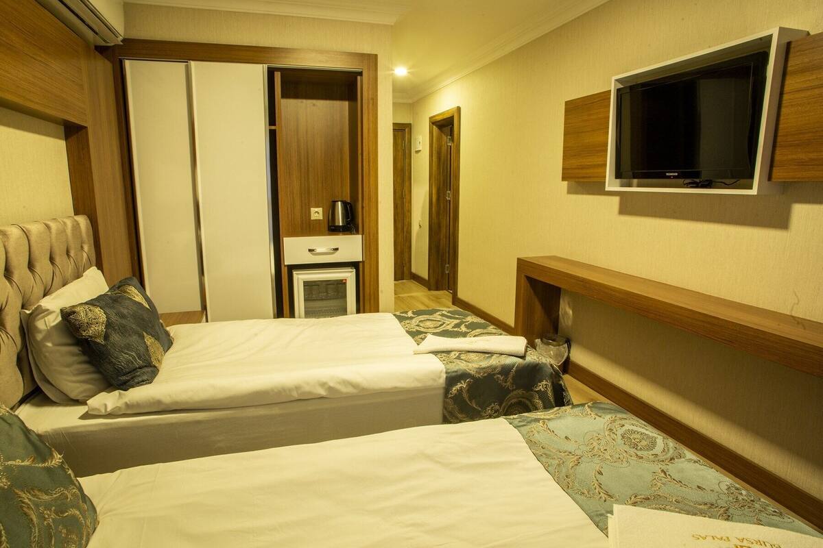 Quarto de hotel com duas camas, televisão, minibar e guarda-roupa de madeira.