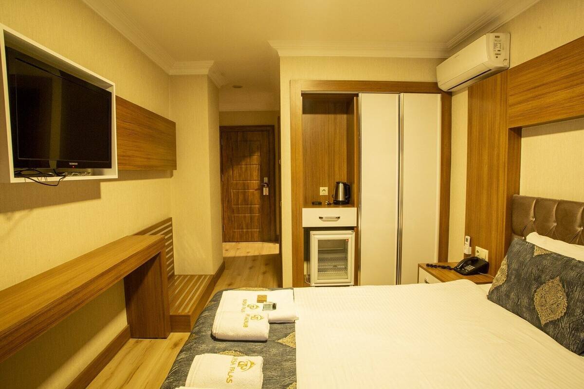 Quarto de hotel com cama, televisão, minibar, cafeteira e telefone.