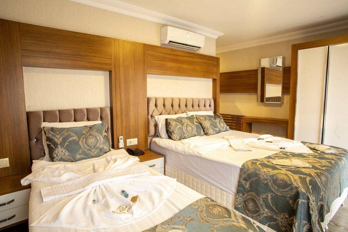 Quarto de hotel com duas camas, uma cabeceira de madeira, uma mesa de cabeceira com telefone e um aparelho de ar condicionado.