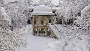 Uma estrutura de pedra coberta de neve com um teto em cúpula, rodeada por árvores carregadas de neve.