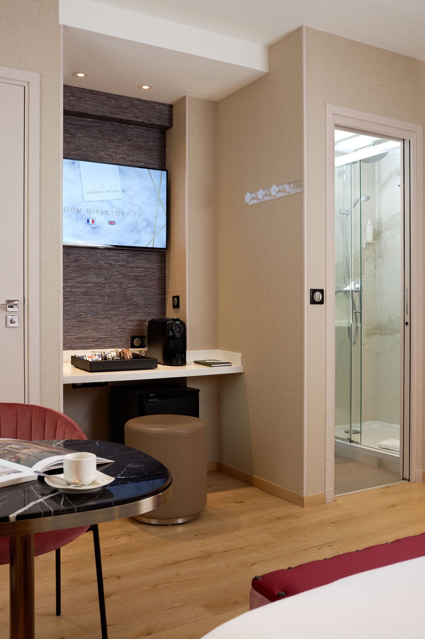 Quarto de hotel com cama, secretária com cafeteira, televisão na parede e zona de chuveiro.