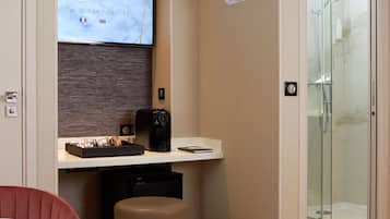 Quarto de hotel com cama, secretária com cafeteira, televisão na parede e zona de chuveiro.
