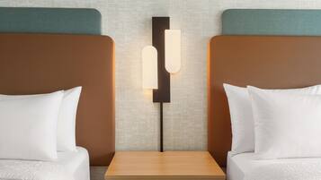 Quarto de hotel com duas camas, uma mesinha de cabeceira e uma luminária fixada na parede.