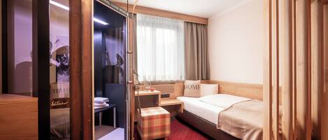 Quarto de hotel com cama, escrivaninha, guarda-roupa e um pequeno banquinho.